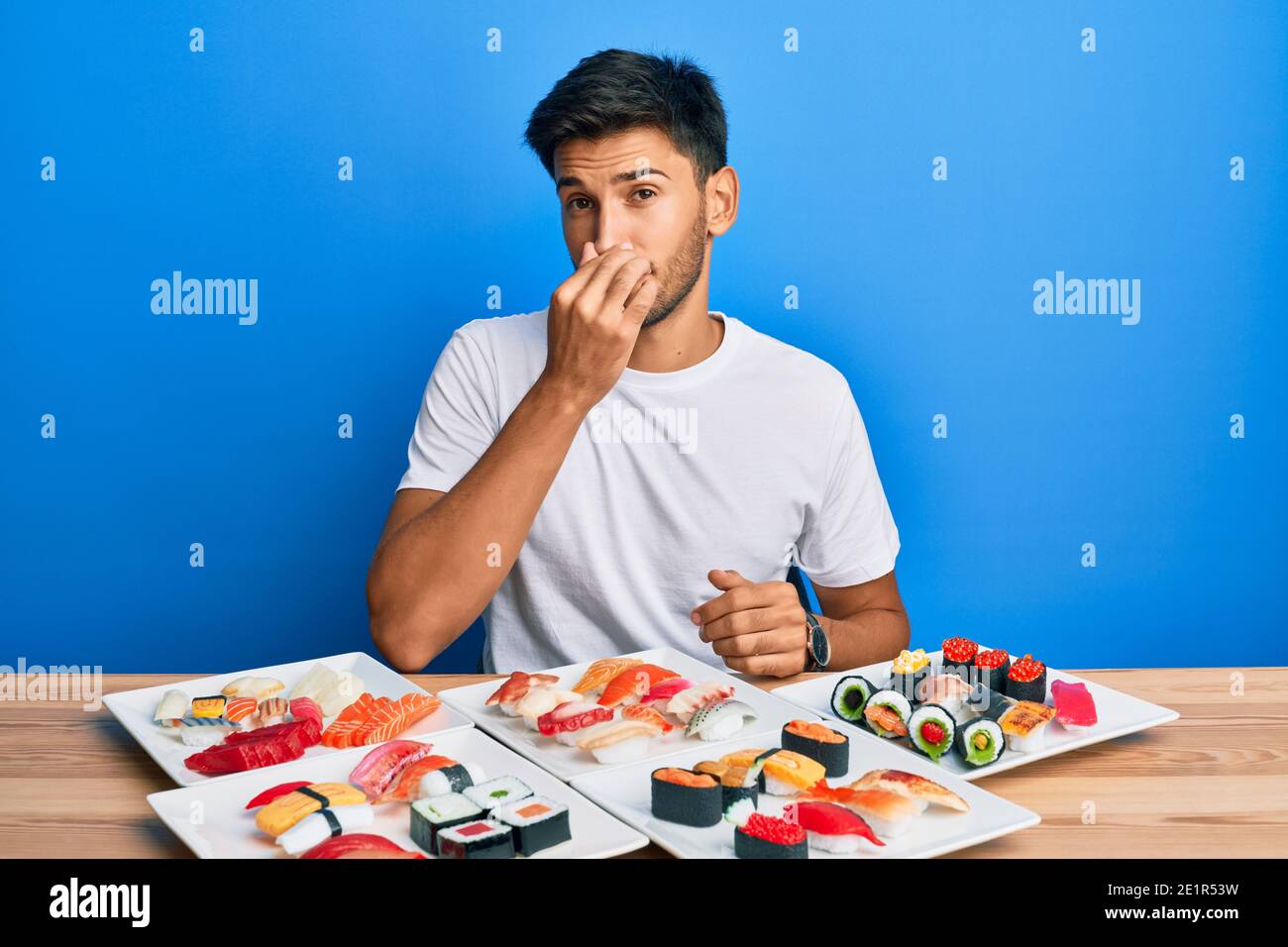 Young handsome man eating sushi sitting on the table smelling something ...