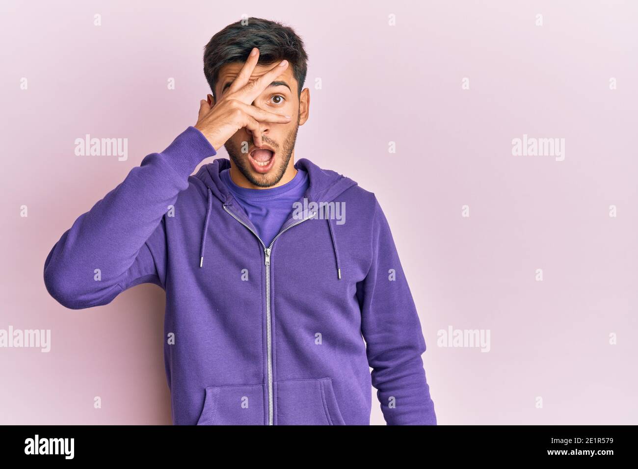 Young handsome man wearing casual sweatshirt peeking in shock covering ...