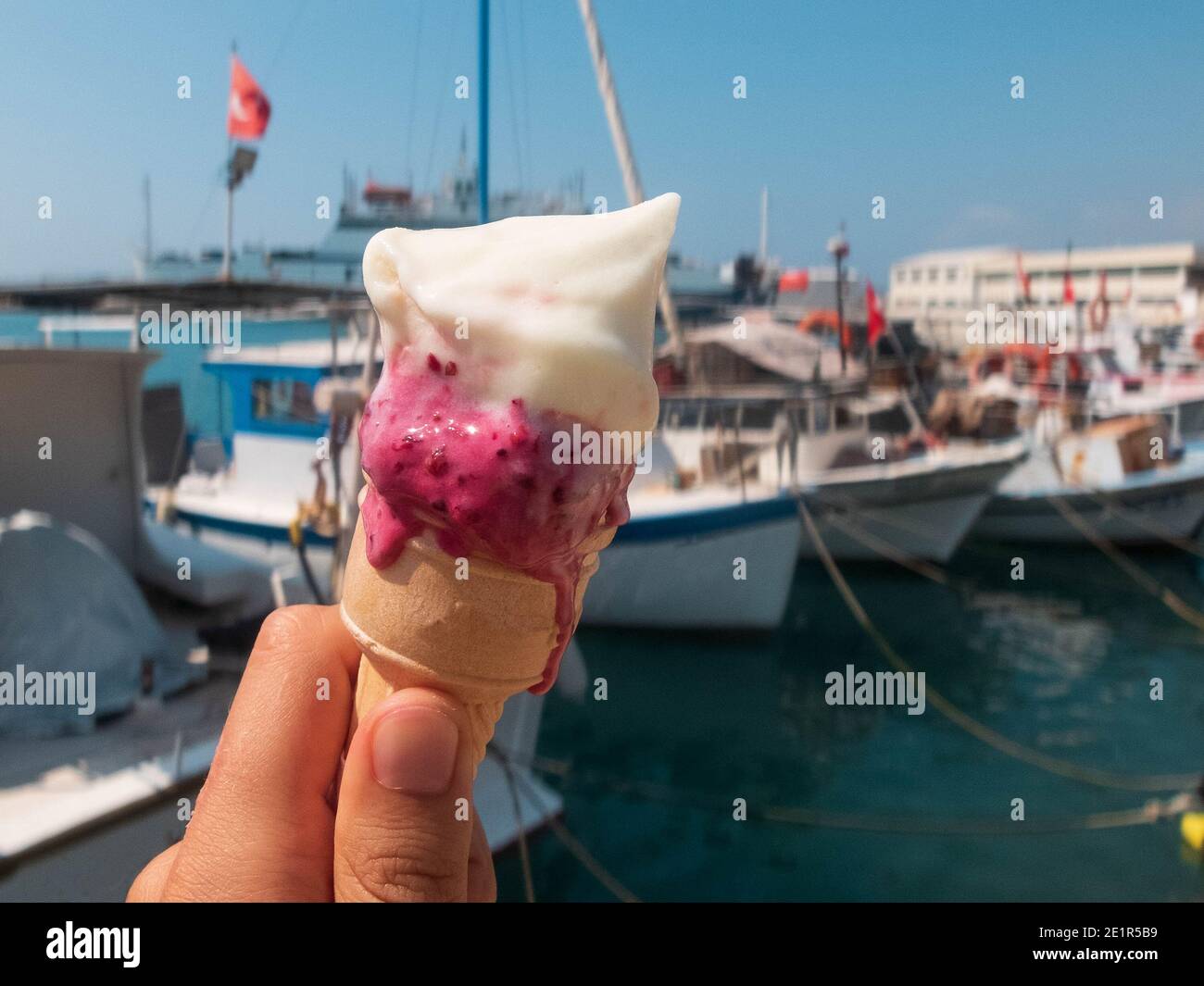Melting ice cream in hand opposite boats at marina. Hot summer concept ...