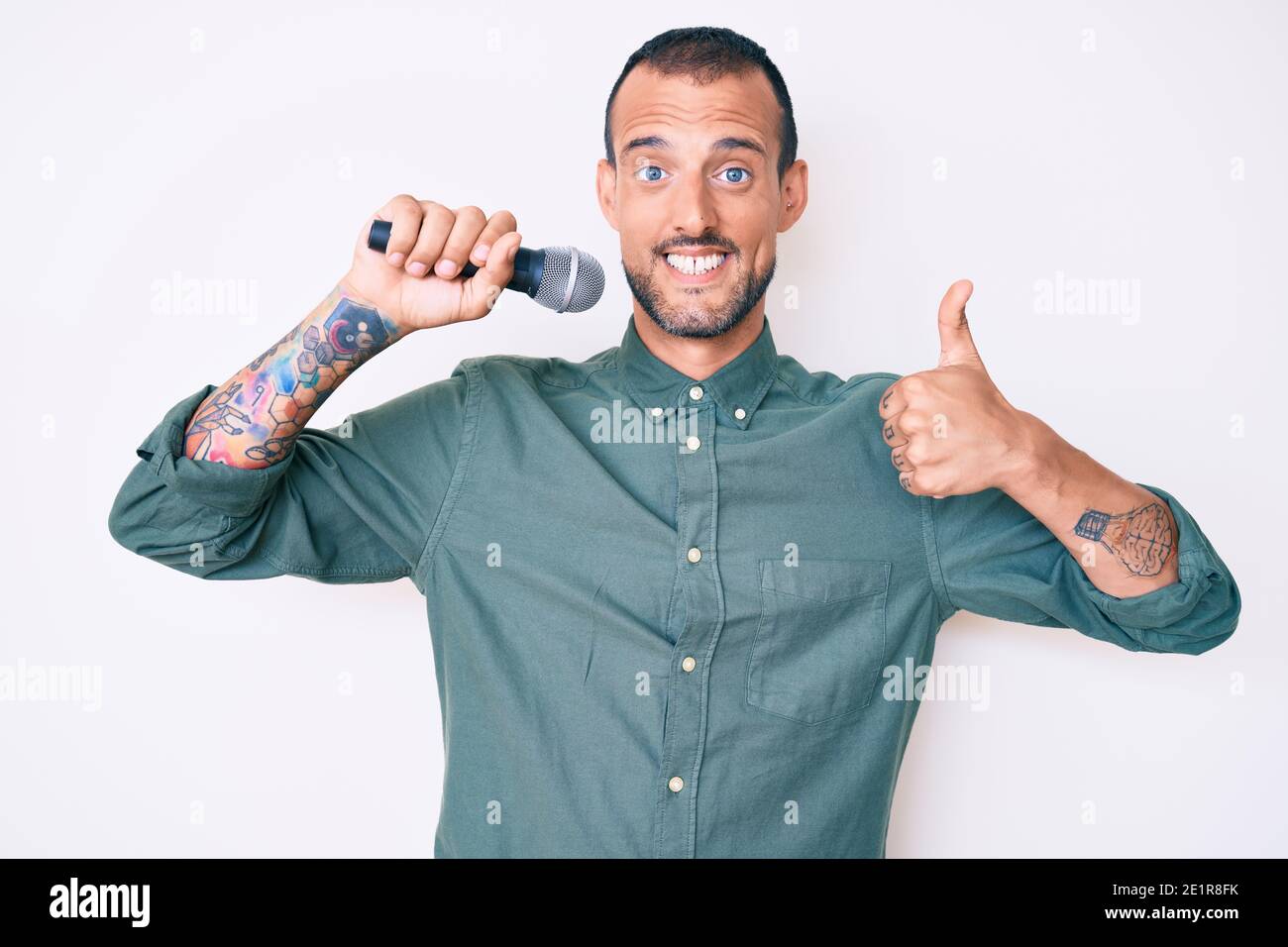 Young handsome man with tattoo singing song using microphone smiling ...