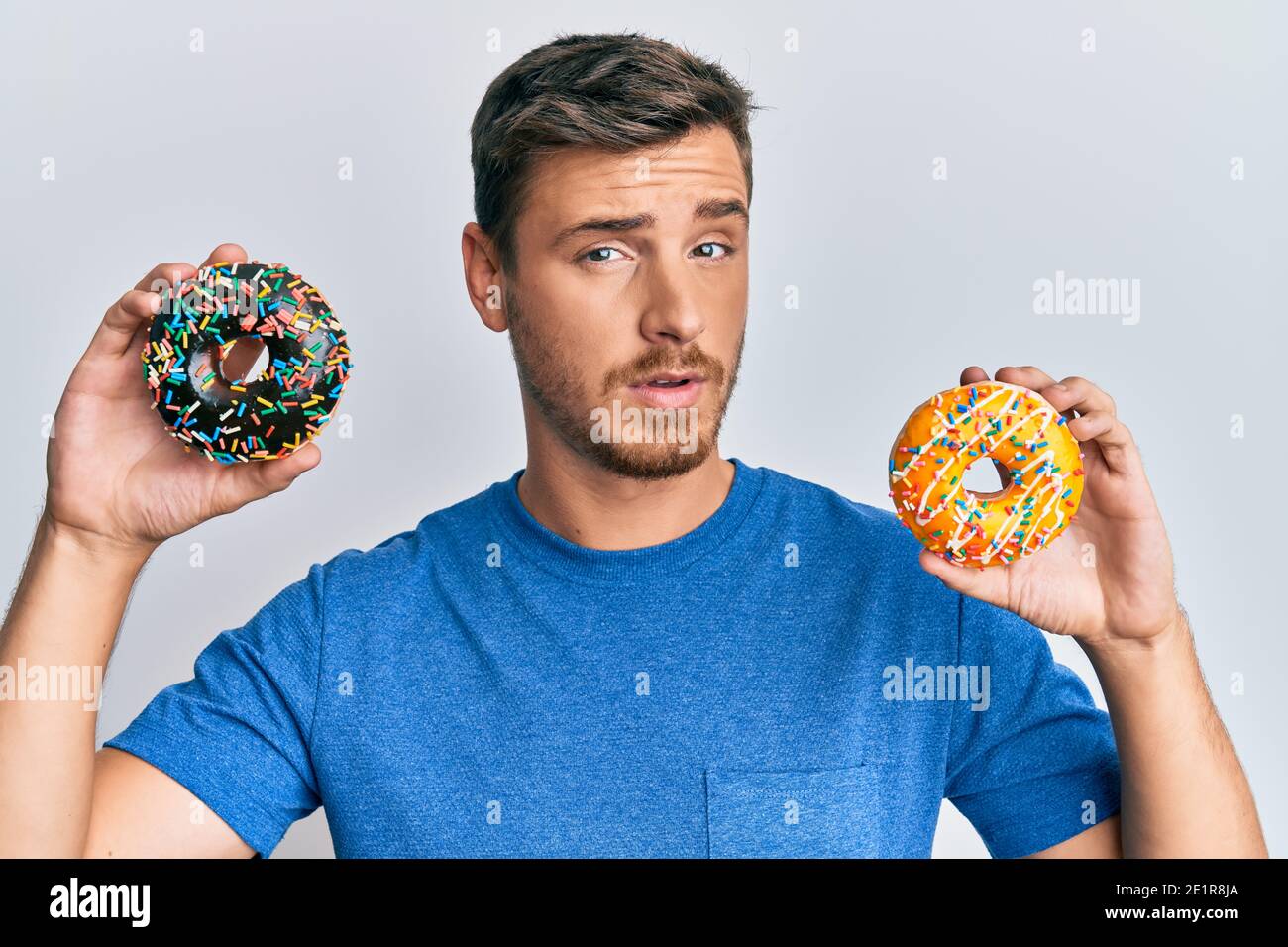 Handsome caucasian man holding tasty colorful doughnuts in shock face ...