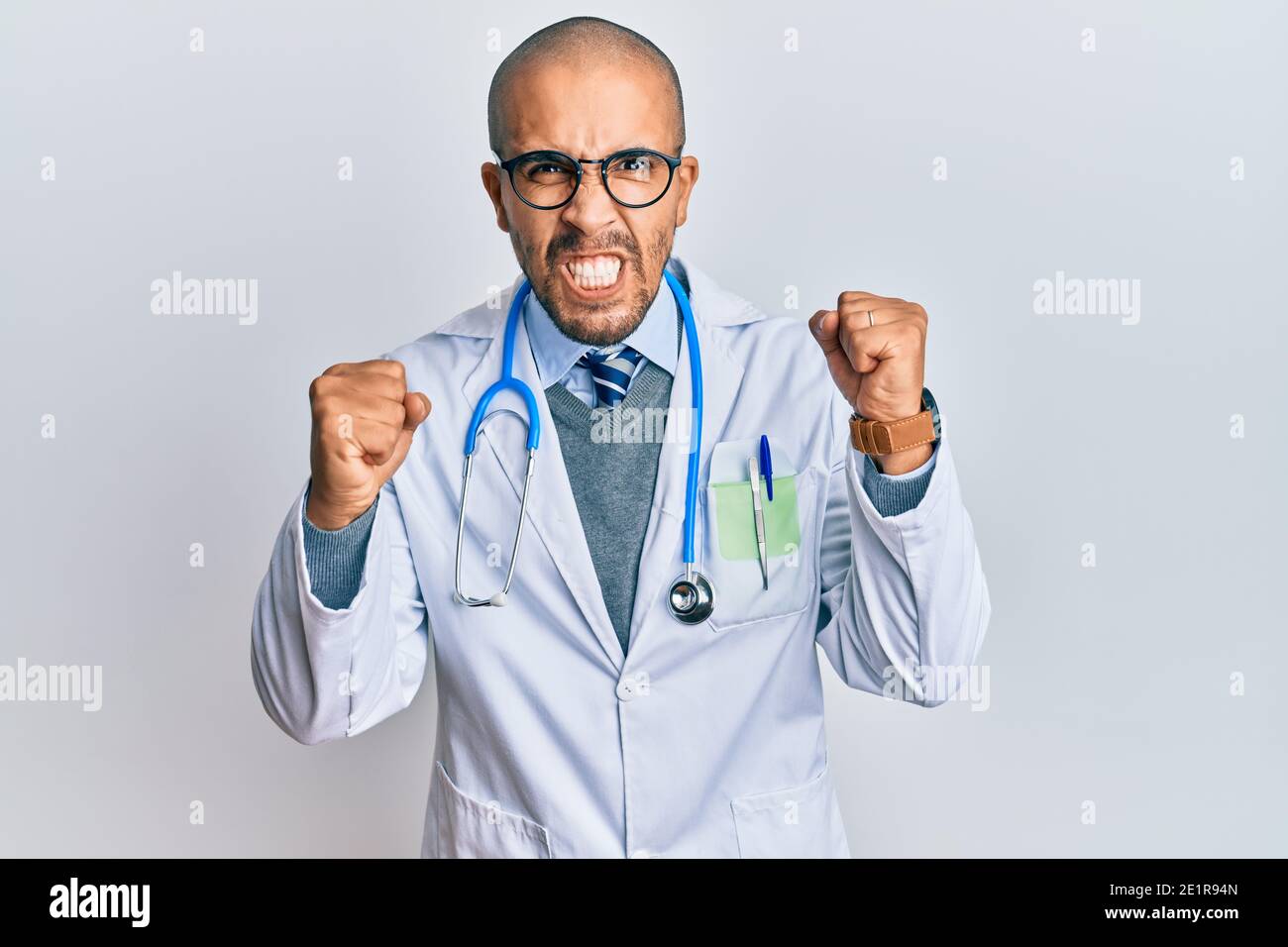 Hispanic adult man wearing doctor uniform and stethoscope angry and mad ...
