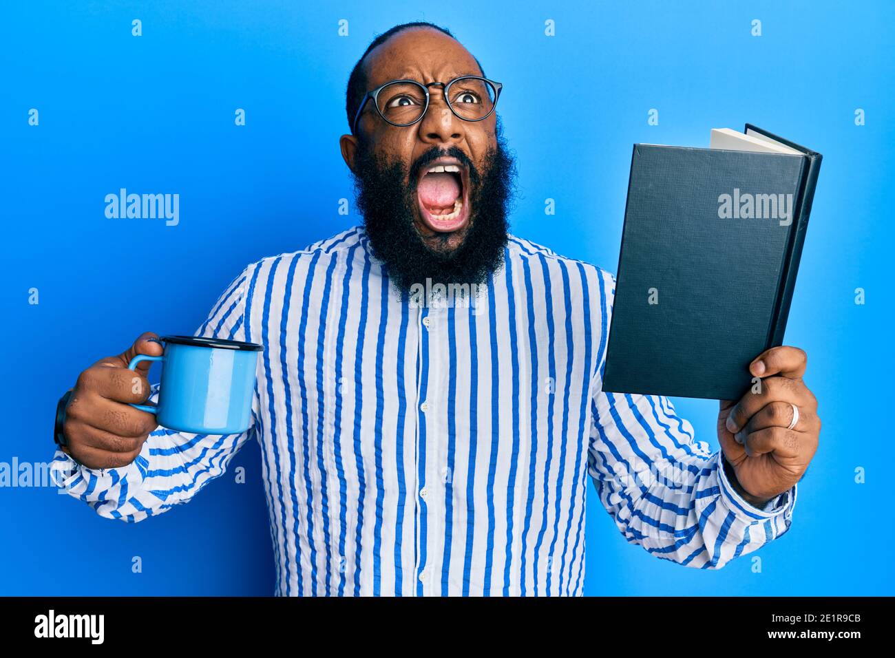 Young african american man reading book and drinking a cup of coffee ...