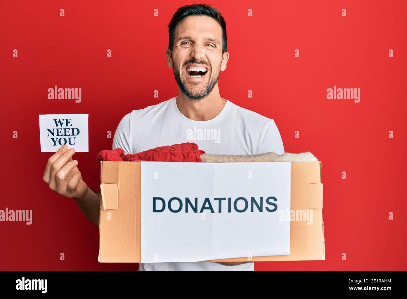Young handsome man holding donations box and we need you paper smiling ...
