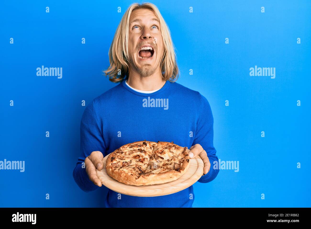 Caucasian young man with long hair holding italian pizza angry and mad ...