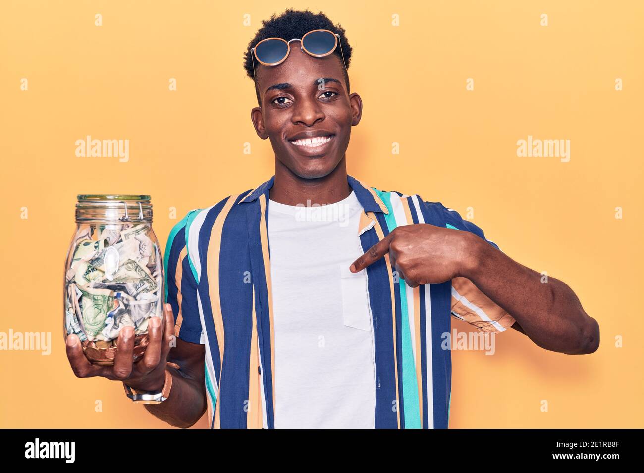 Young african american man holding jar with savings pointing finger to ...