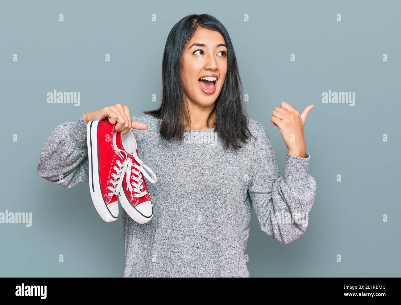 Beautiful asian young woman holding red casual shoes pointing thumb up ...