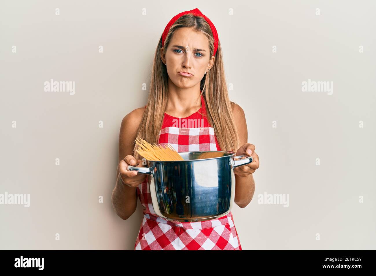 Young blonde woman wearing professional baker apron holding cooking pot ...