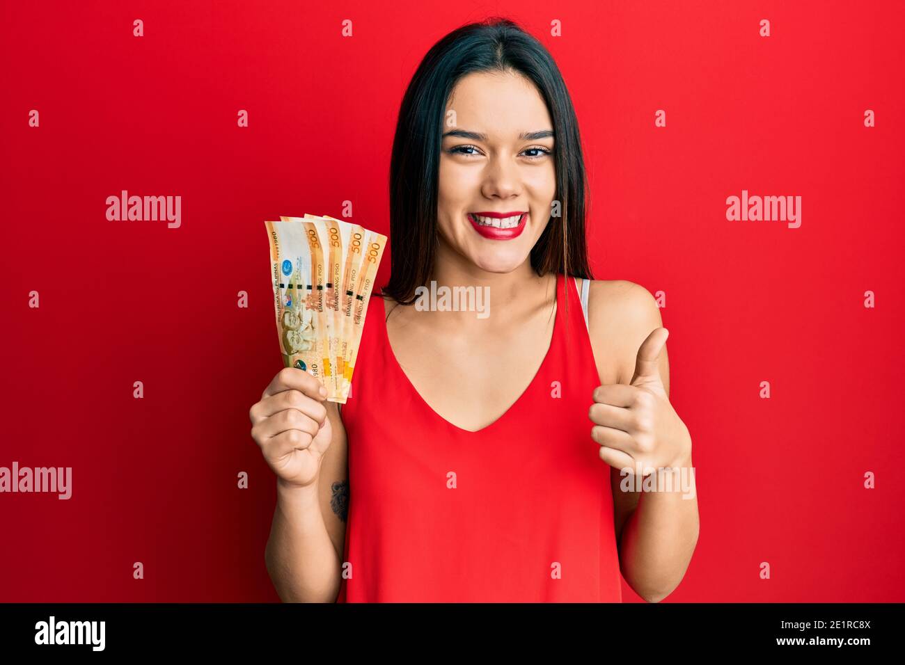 Young hispanic girl holding 500 philippine peso banknotes smiling happy ...