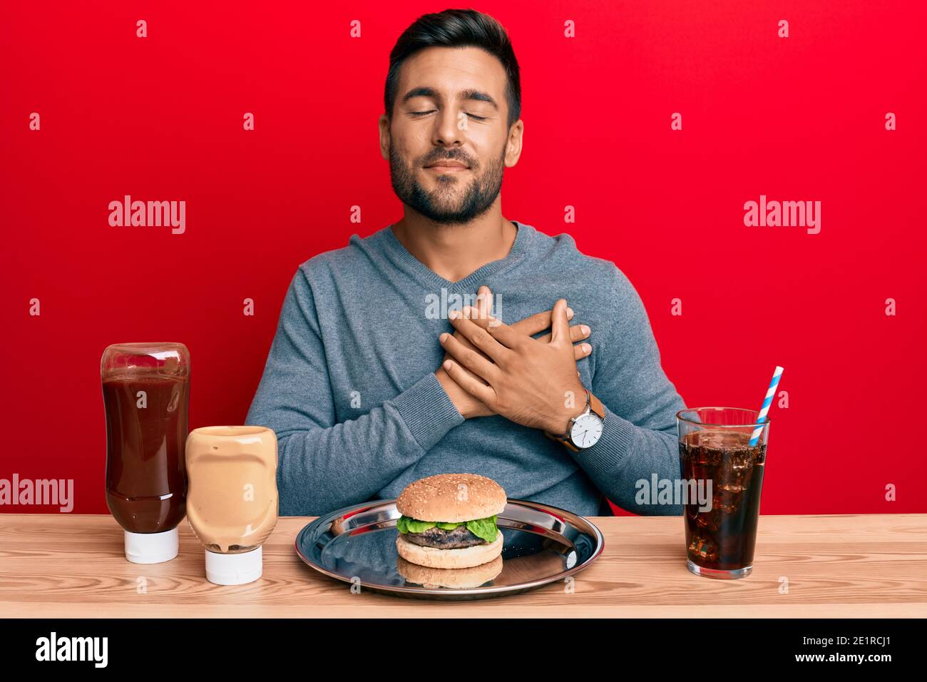 Handsome hispanic man eating a tasty classic burger and soda smiling ...