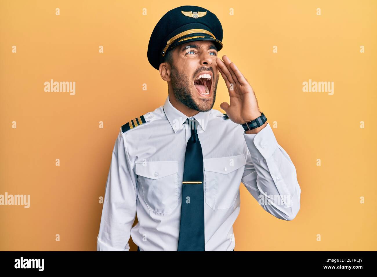 Handsome hispanic man wearing airplane pilot uniform shouting and ...