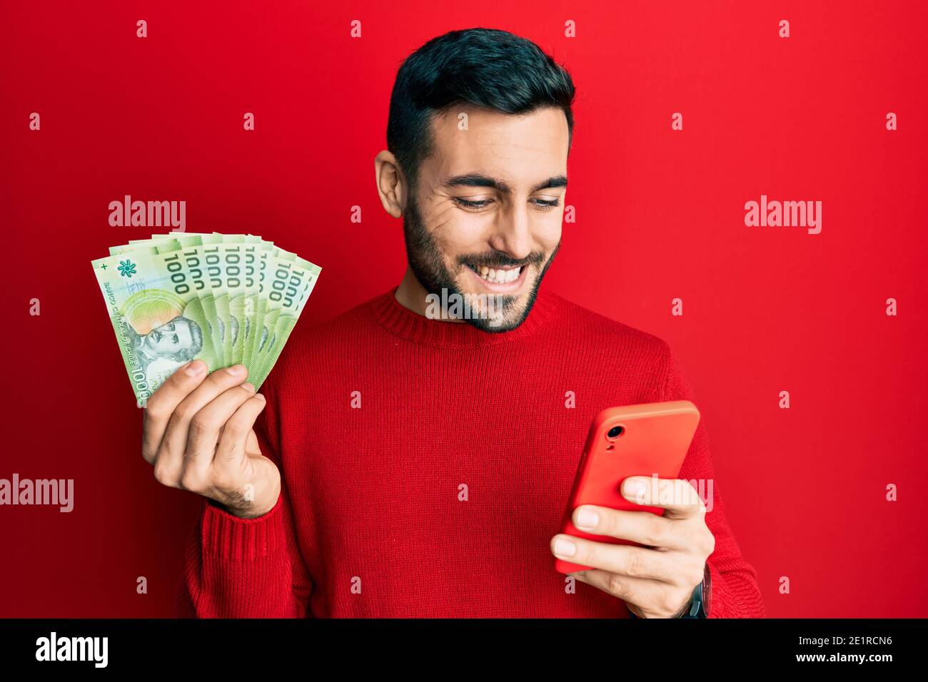Young hispanic man using smartphone holding chilean pesos banknotes ...