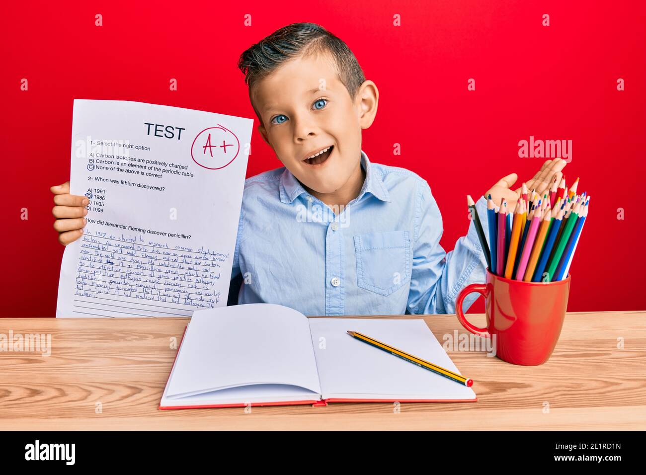 Adorable caucasian kid holding passed test sitting on the table ...