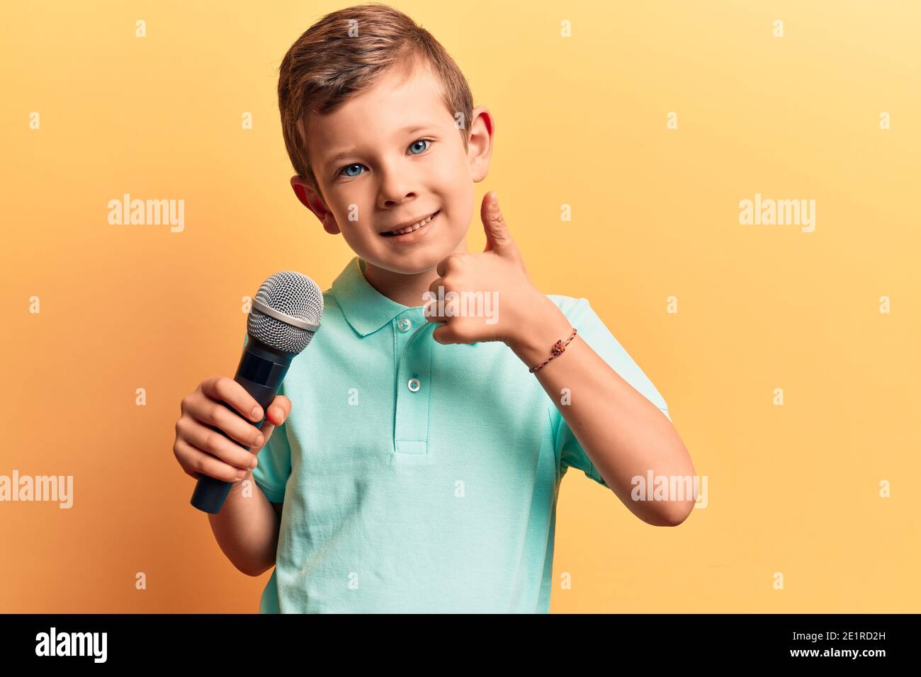 Cute blond kid singing song using microphone smiling happy and positive ...