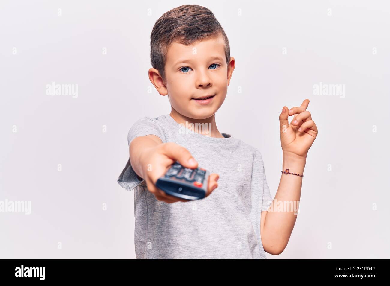 Cute blond kid holding television remote control smiling happy pointing ...