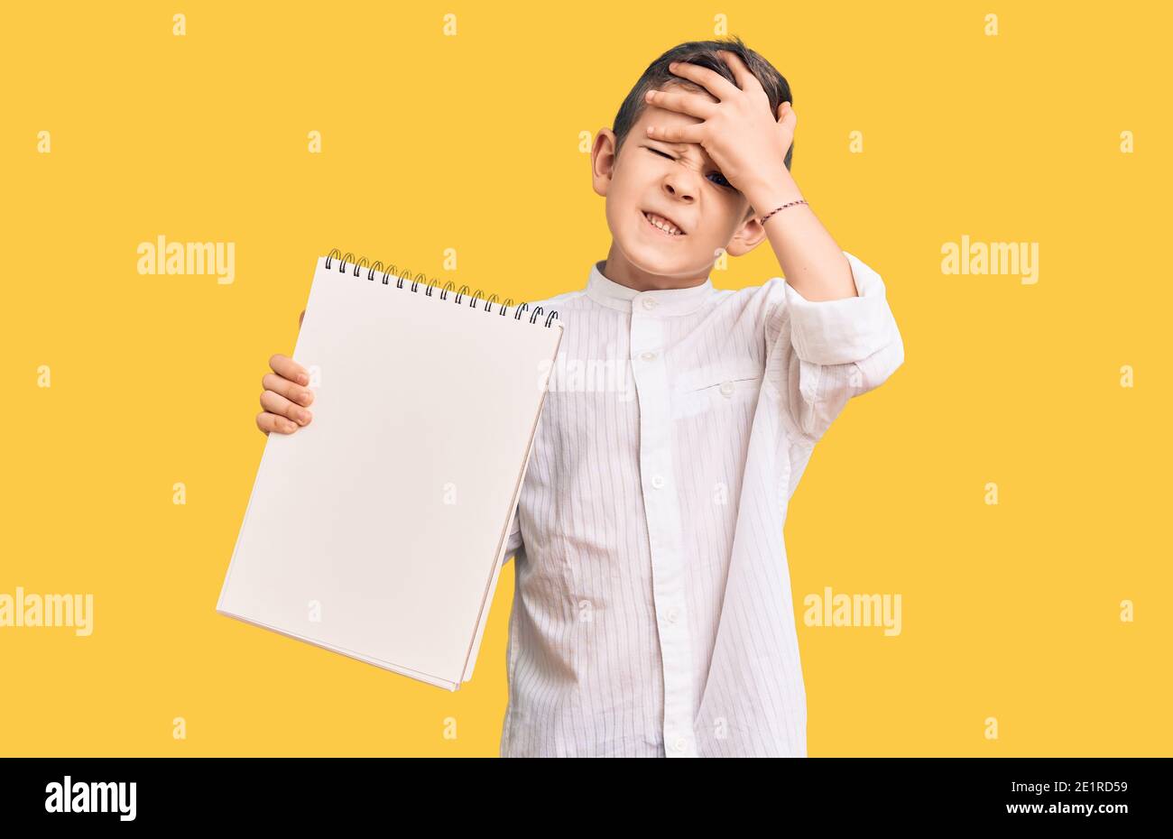 Cute blond kid holding notebook stressed and frustrated with hand on ...
