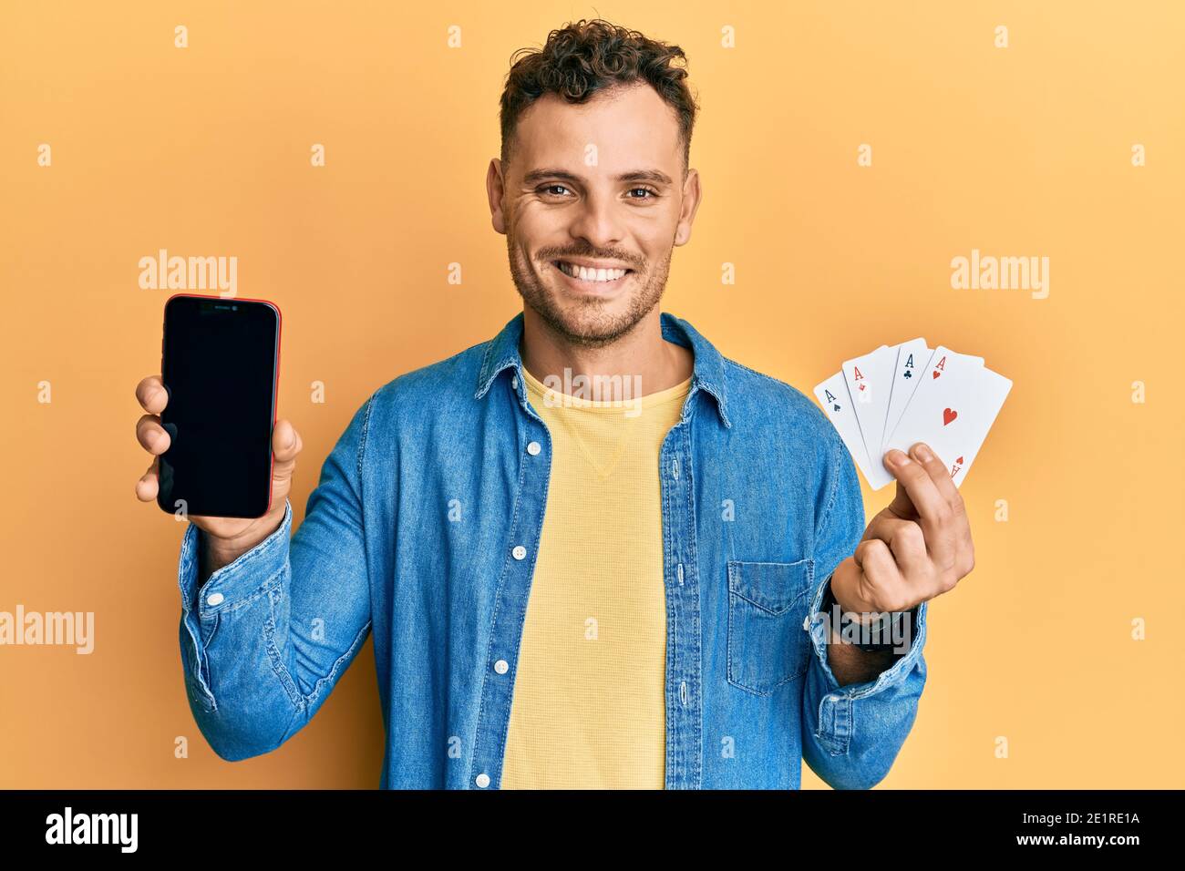 Young hispanic man holding poker cards and smartphone showing blank ...