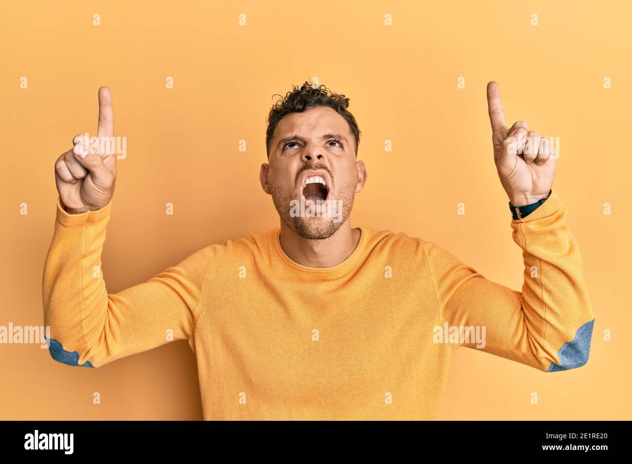 Young hispanic man pointing up with fingers angry and mad screaming ...