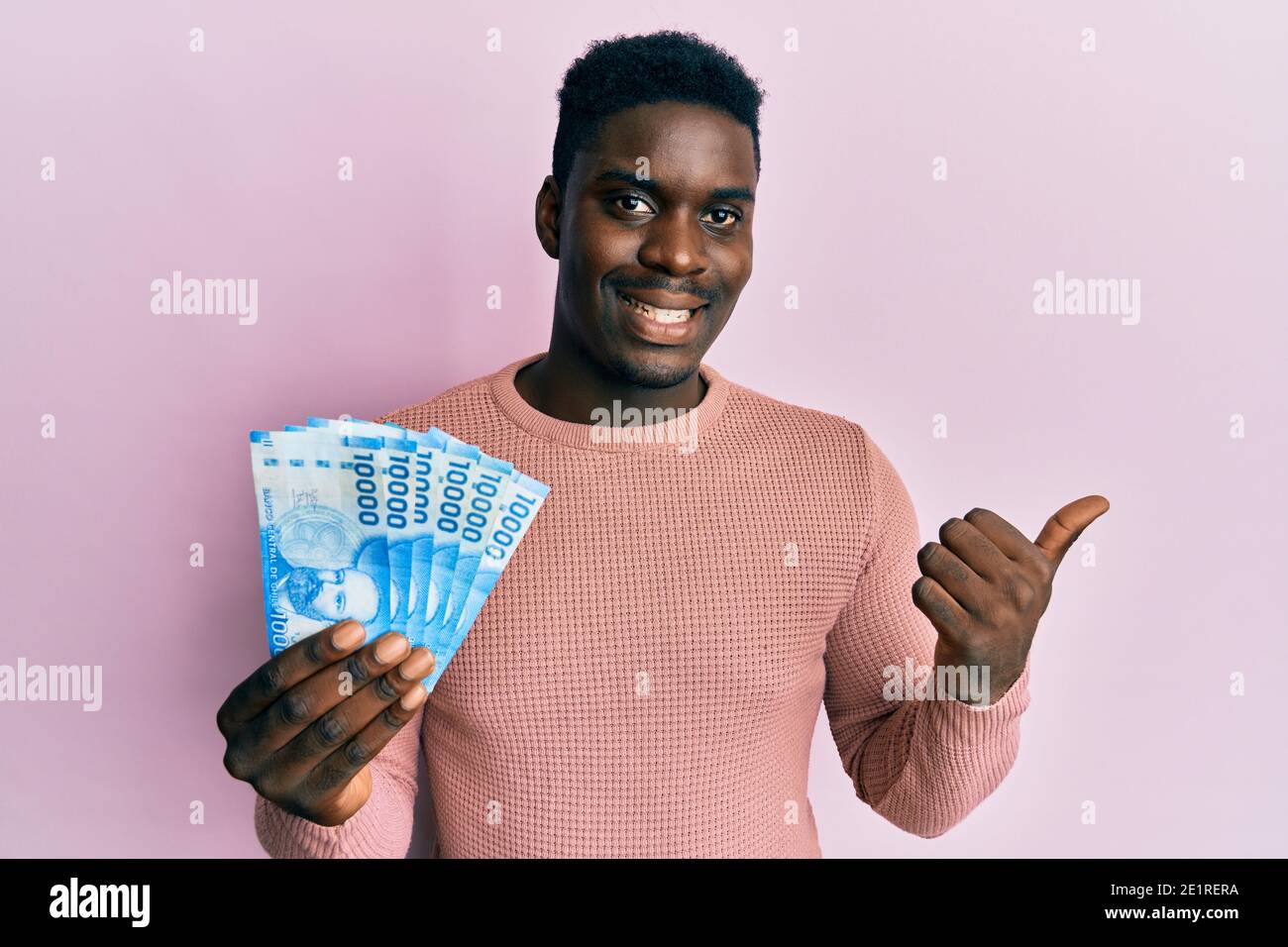 Handsome black man holding 10000 chilean pesos pointing thumb up to the ...