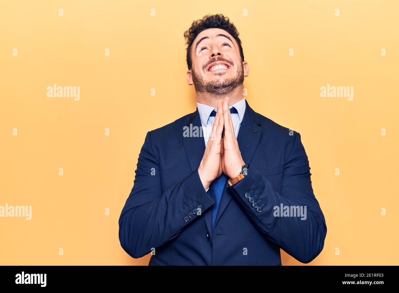 Young hispanic man wearing suit begging and praying with hands together ...