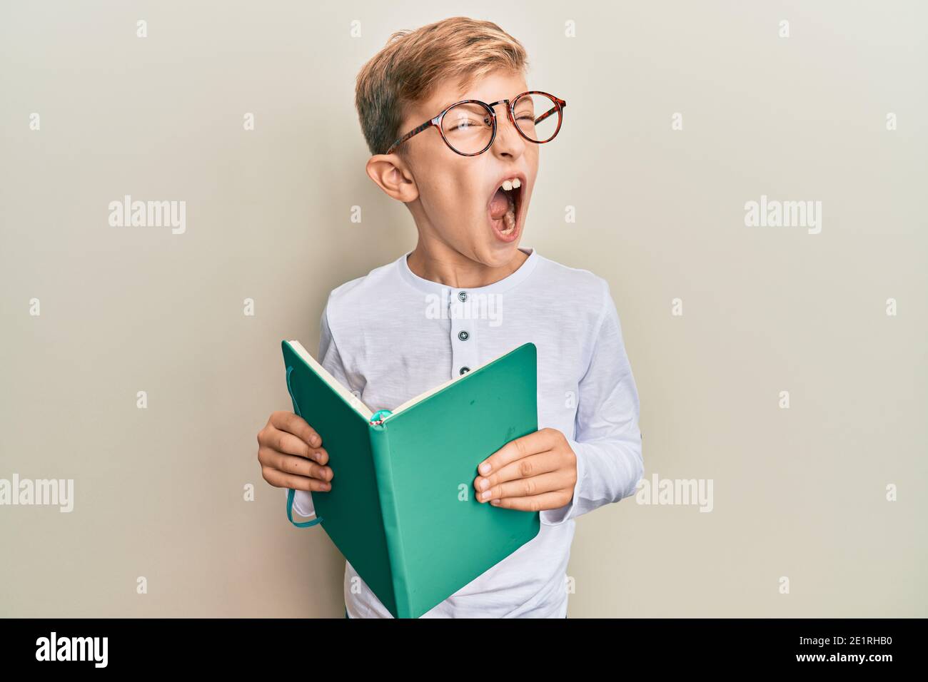 Little caucasian boy kid reading a book wearing glasses angry and mad ...