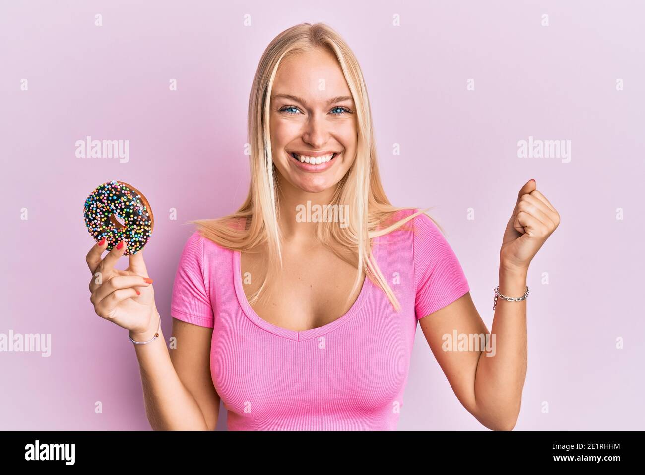 Young blonde girl holding donut screaming proud, celebrating victory ...