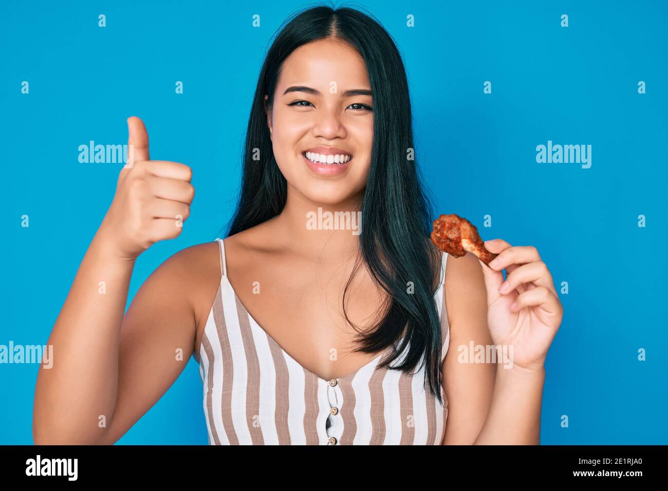 Young asian girl eating chicken wings smiling happy and positive, thumb ...
