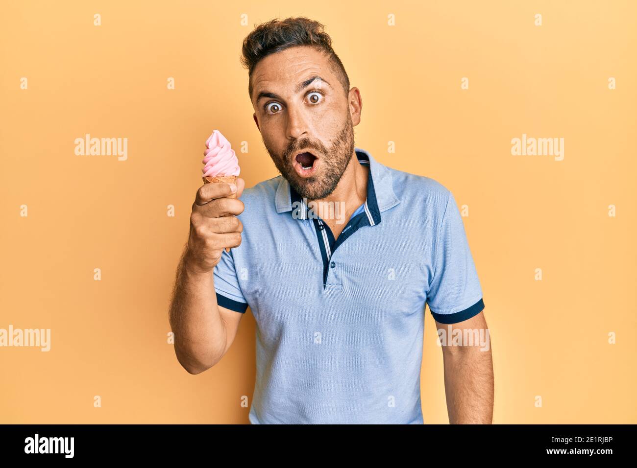 Handsome man with beard eating ice cream cone scared and amazed with ...
