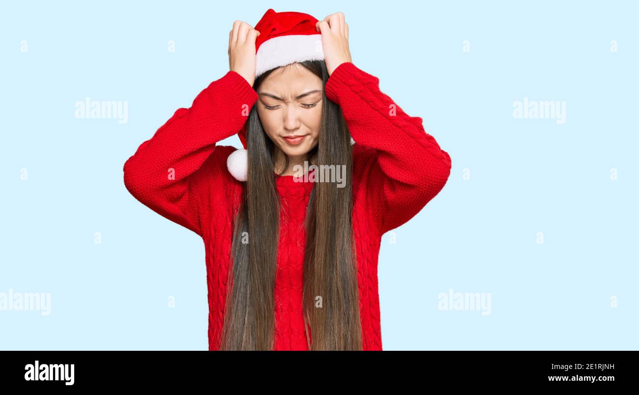 Young chinese woman wearing christmas hat suffering from headache ...