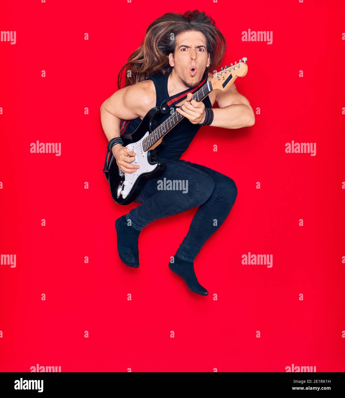 Young handsome man with long hair and aggressive expression playing ...