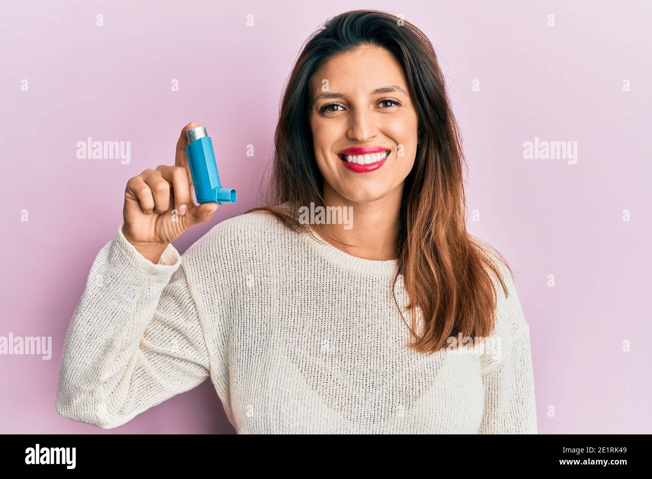 Beautiful hispanic woman holding medical asthma inhaler looking ...