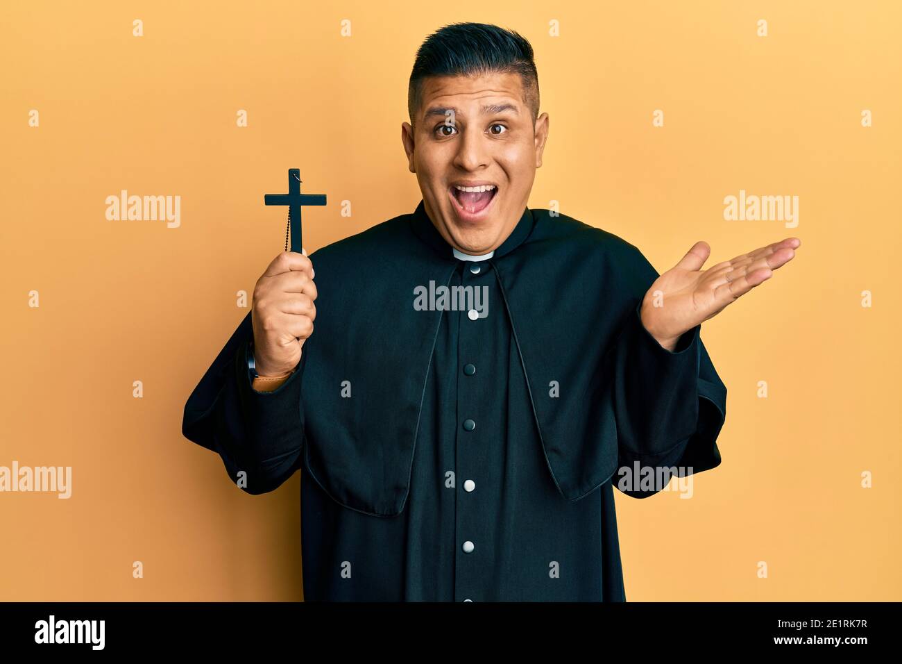 Young latin priest man holding crucifix celebrating achievement with ...