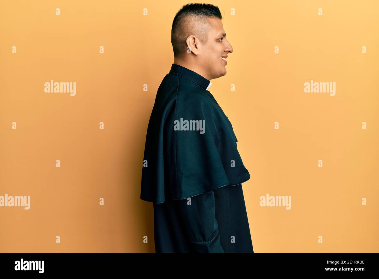 Young latin priest man standing over yellow background looking to side ...