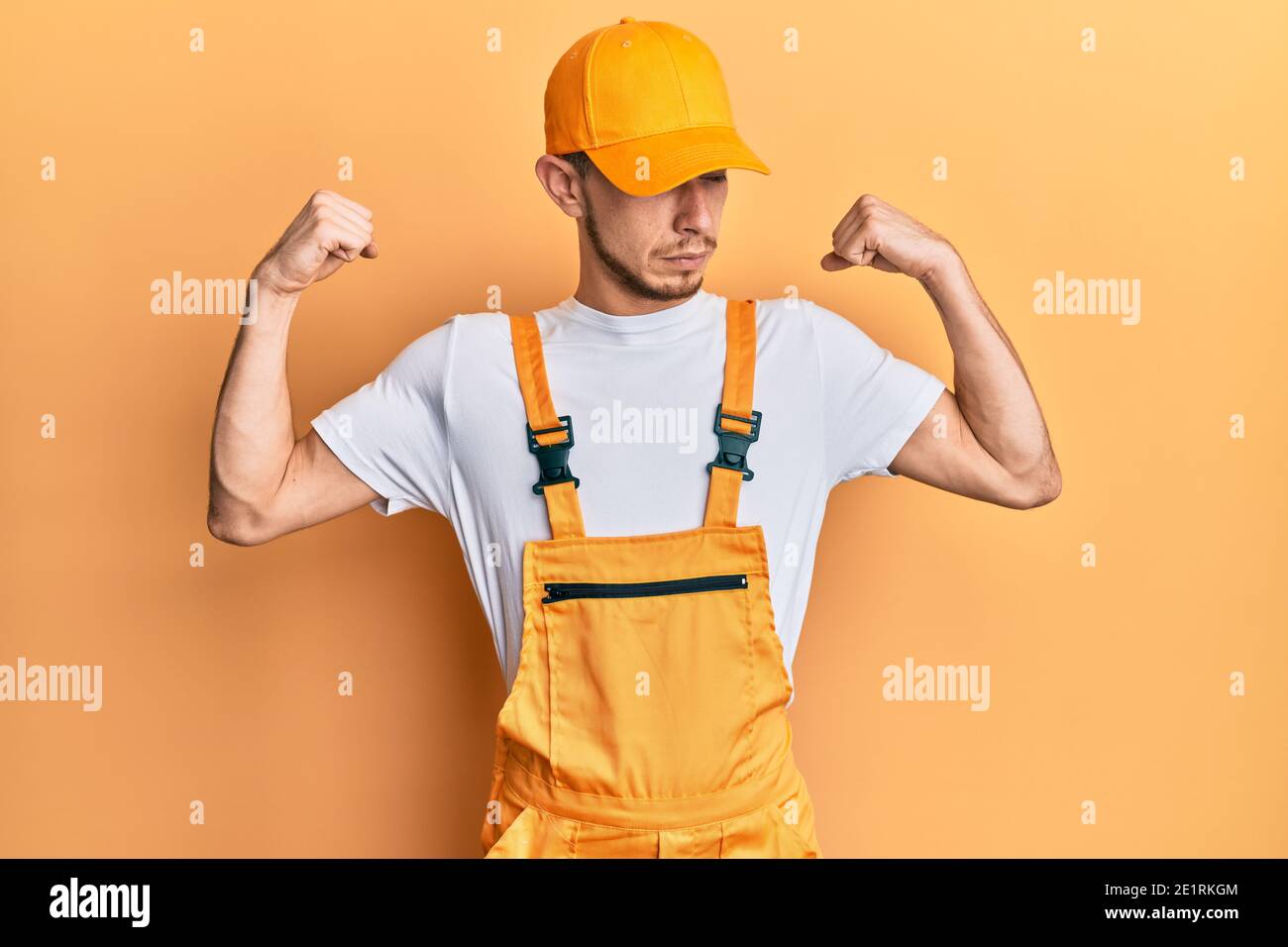 Hispanic young man wearing handyman uniform showing arms muscles ...