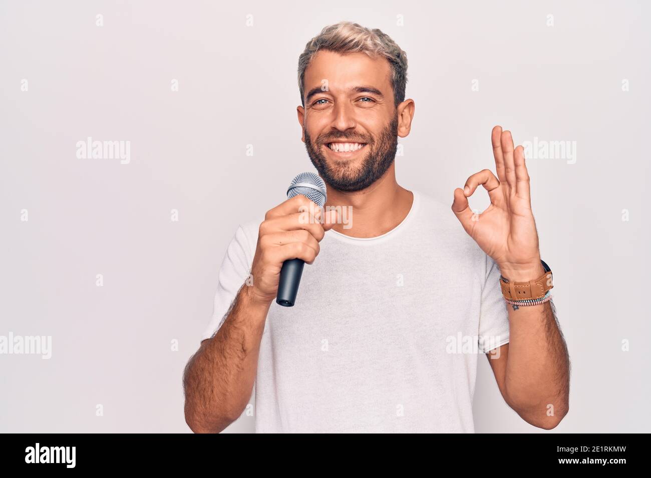 Handsome blond singer man with beard singing song using microphone over white background doing ...