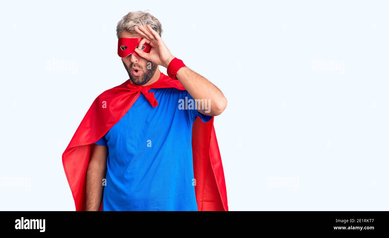 Young blond man wearing super hero custome doing ok gesture shocked ...