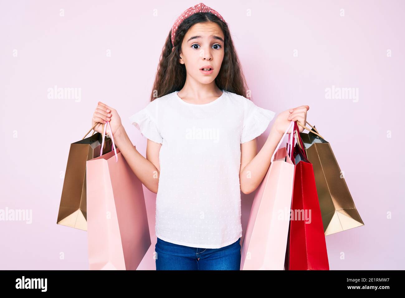 Cute hispanic girl holding shopping bags clueless and confused ...