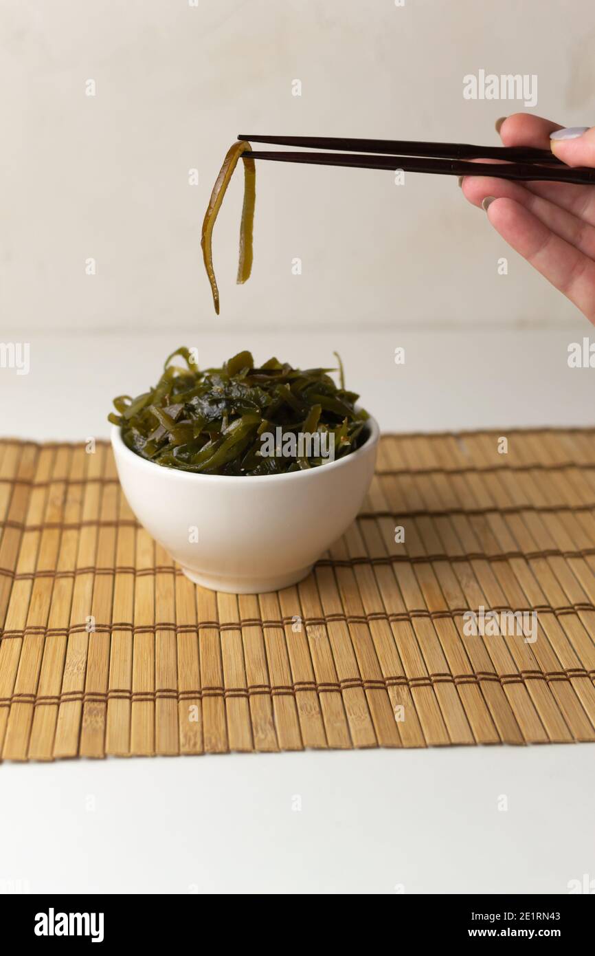 Edible seaweed in a white bowl on a bamboo rug. Vegetarian food concept ...