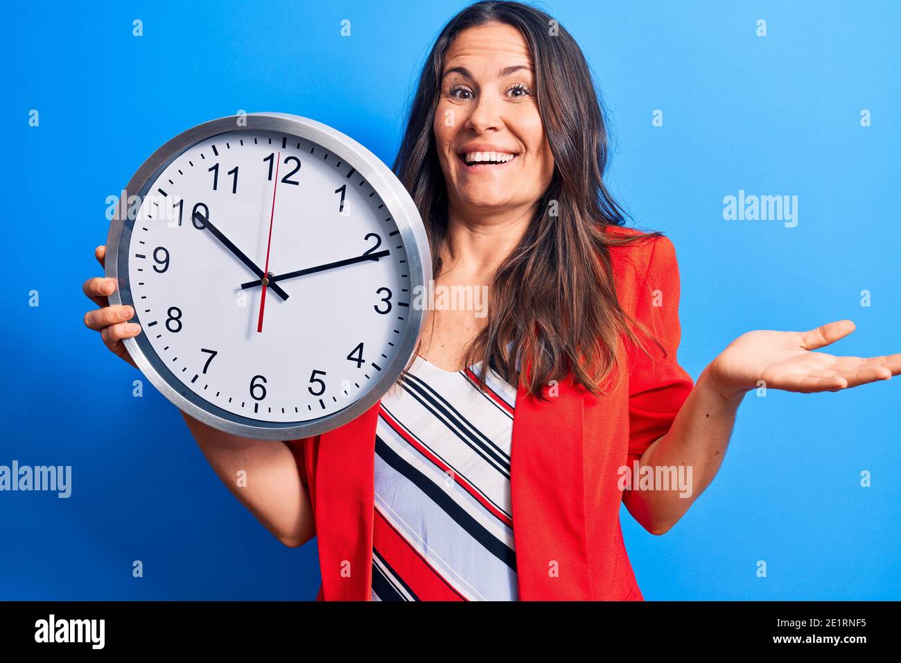 Young beautiful brunette woman doing countdown holding big clock over ...