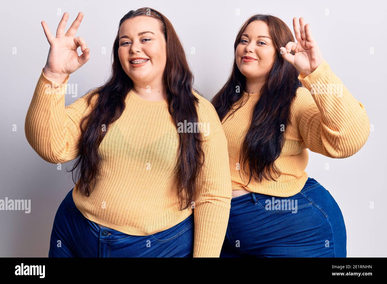 Young plus size twins wearing casual clothes smiling positive doing ok ...