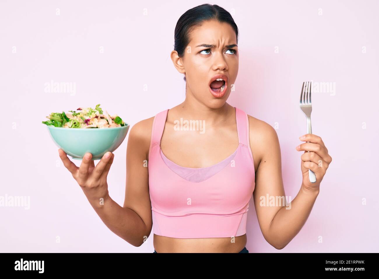 Young beautiful latin girl wearing sportswear holding salad angry and ...