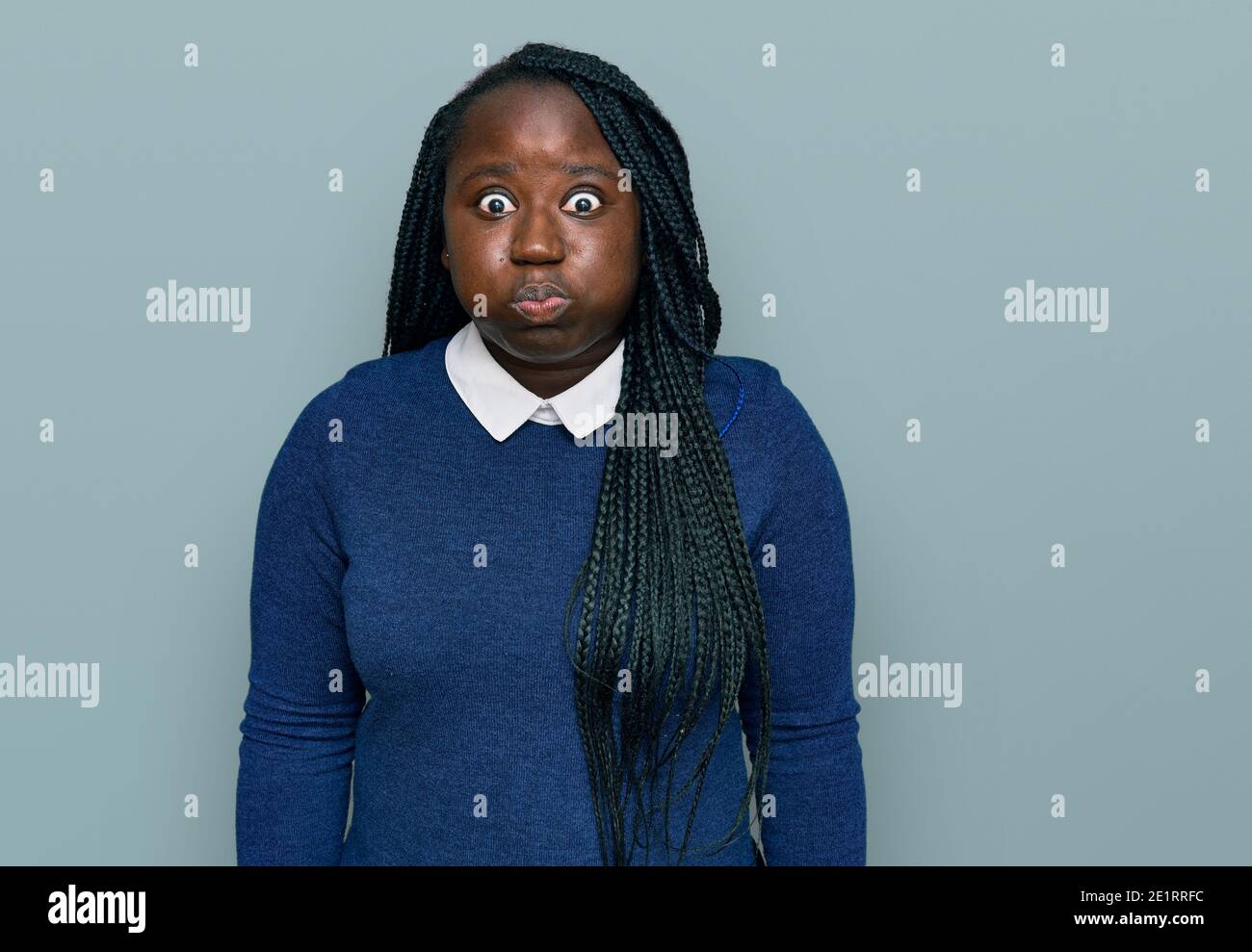 Young black woman with braids wearing casual clothes puffing cheeks ...
