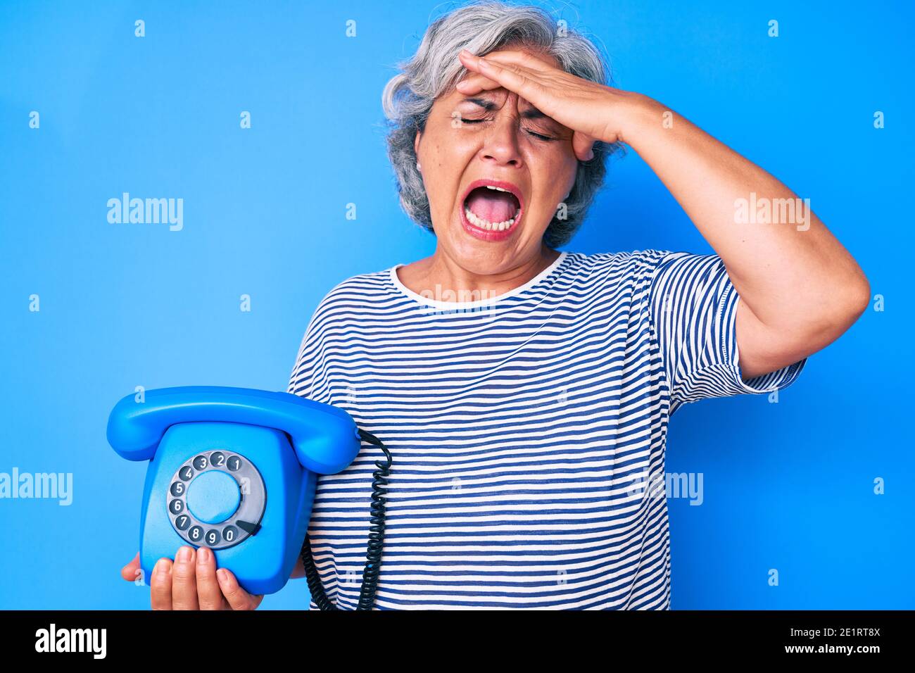 Senior hispanic grey- haired woman holding vintage telephone stressed ...