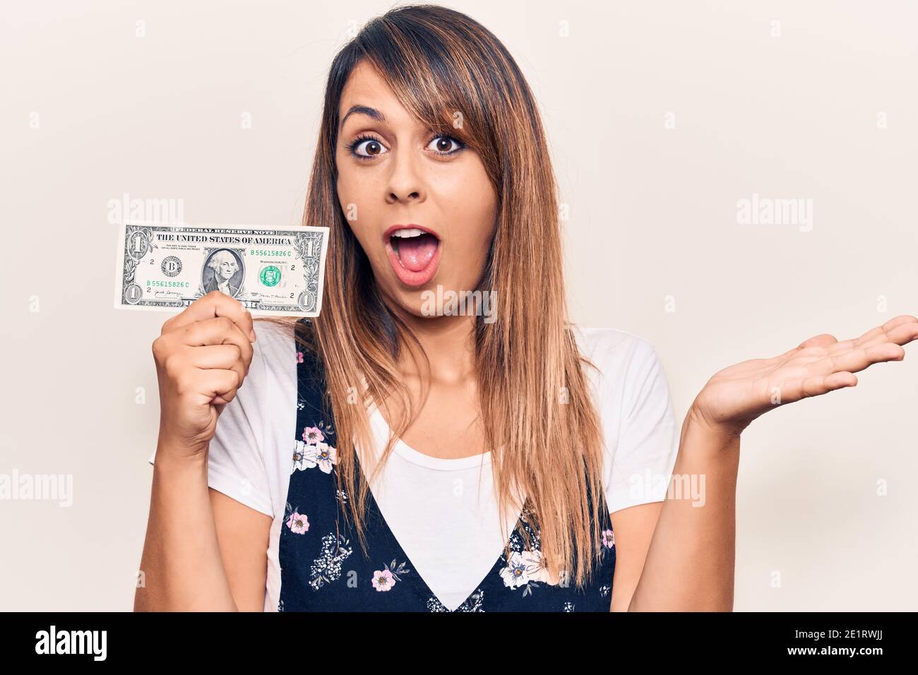 Young beautiful woman holding one dollar celebrating achievement with ...