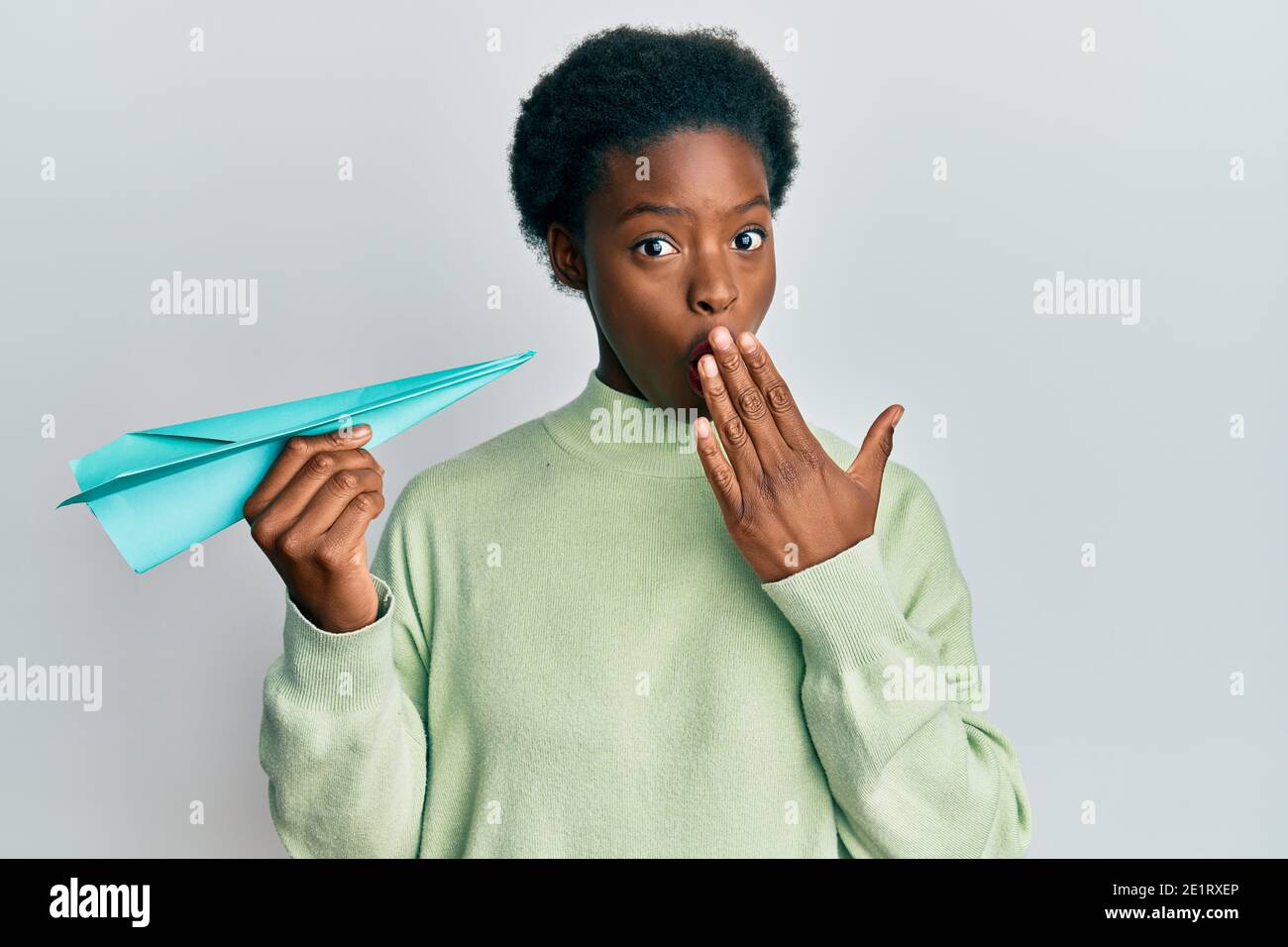 Young african american girl holding paper airplane covering mouth with ...