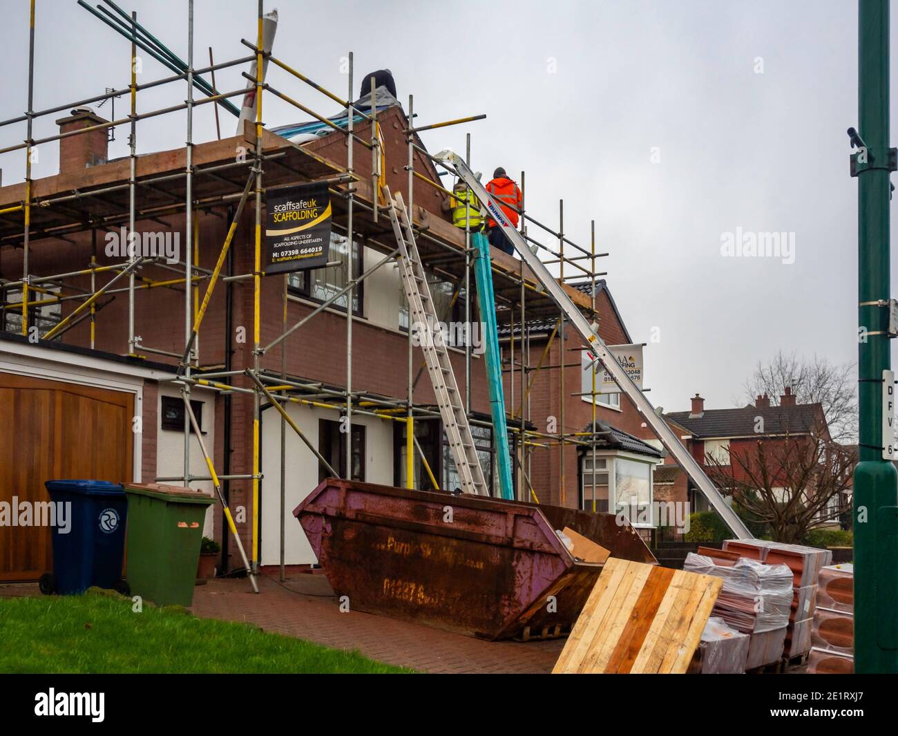 Roofers on scaffolding replacing the tiled roof on a detached house in ...