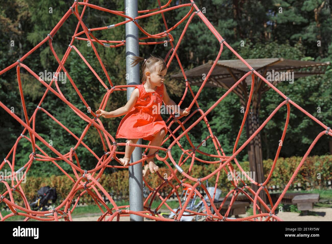Happy little three-year-old child in a red dress in a rope spider web ...
