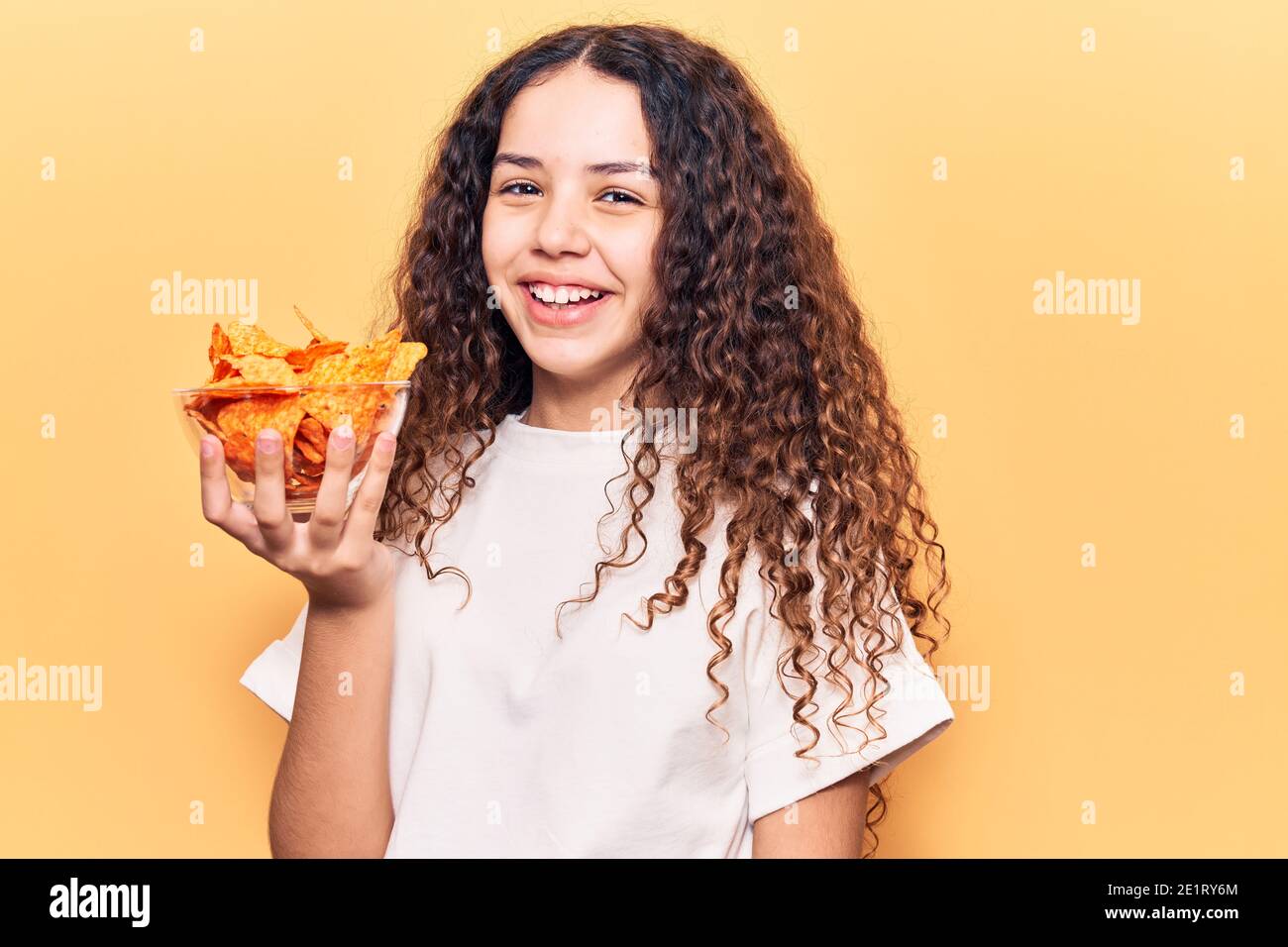 Beautiful kid girl with curly hair holding nachos potato chips looking ...