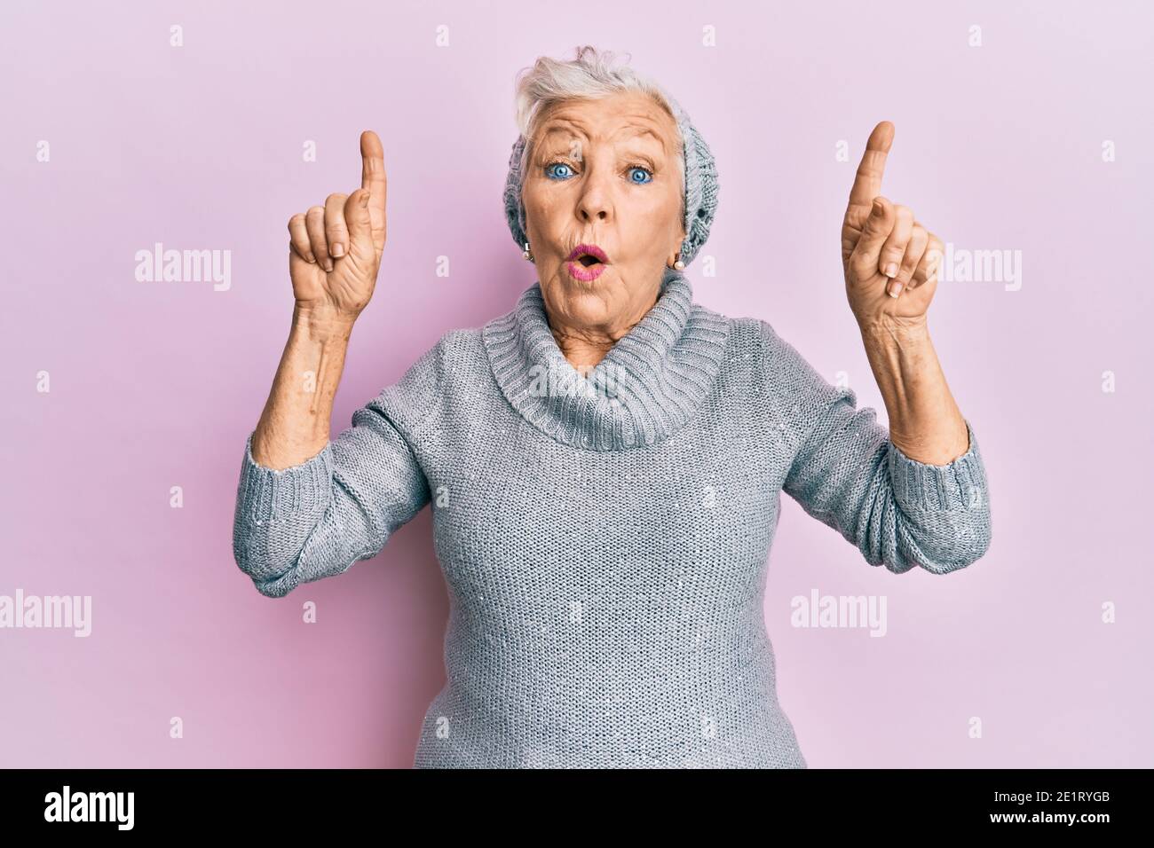 Senior grey-haired woman pointing up with fingers afraid and shocked ...