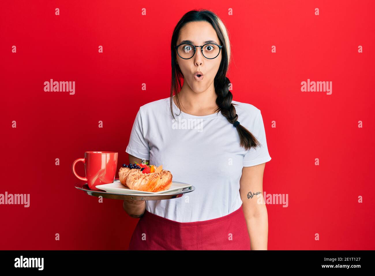 Young hispanic woman wearing waitress apron holding tray with breakfast ...